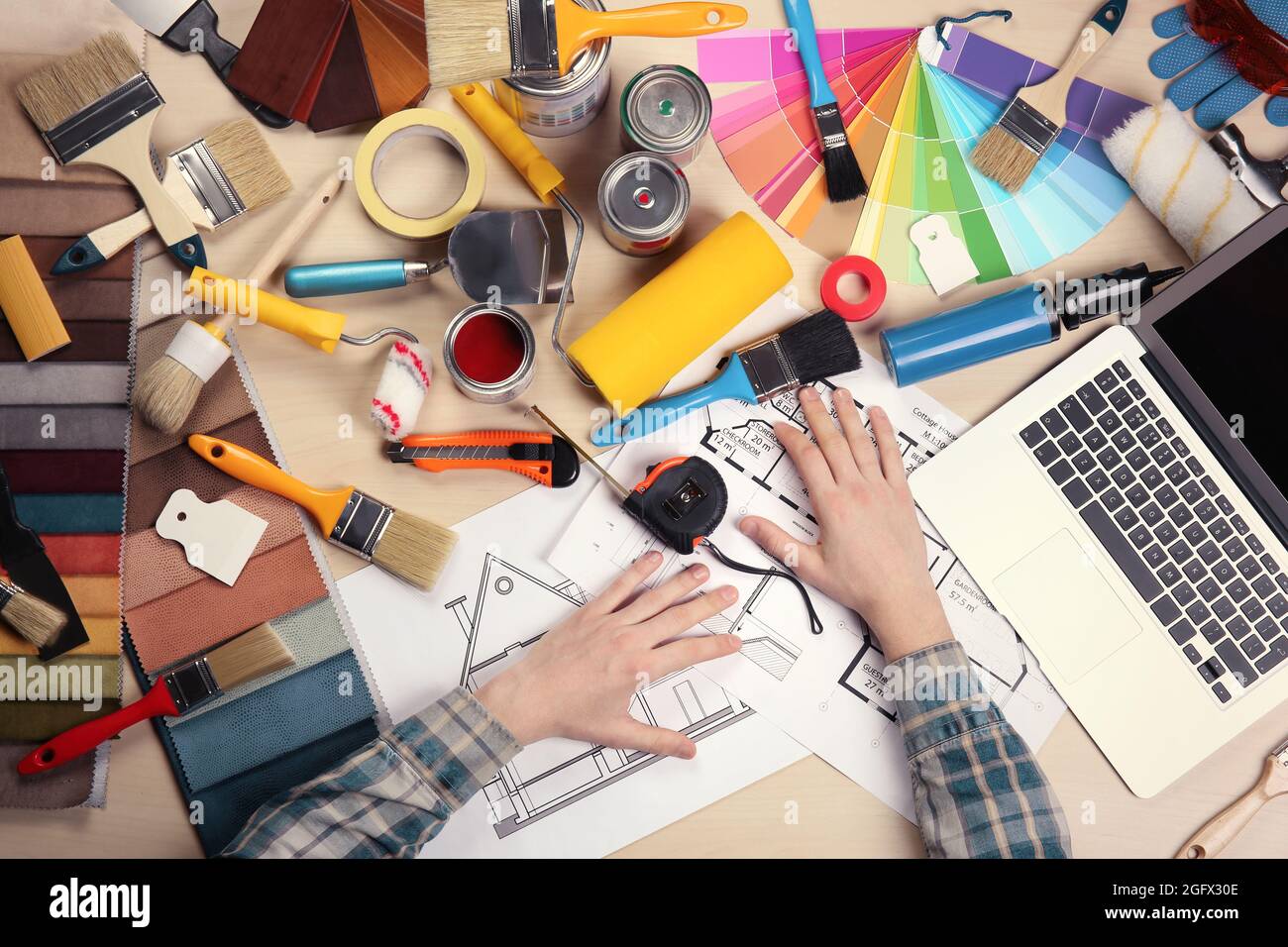 Decorator's hands on project drawings. Laptop, color swatches and tools ...