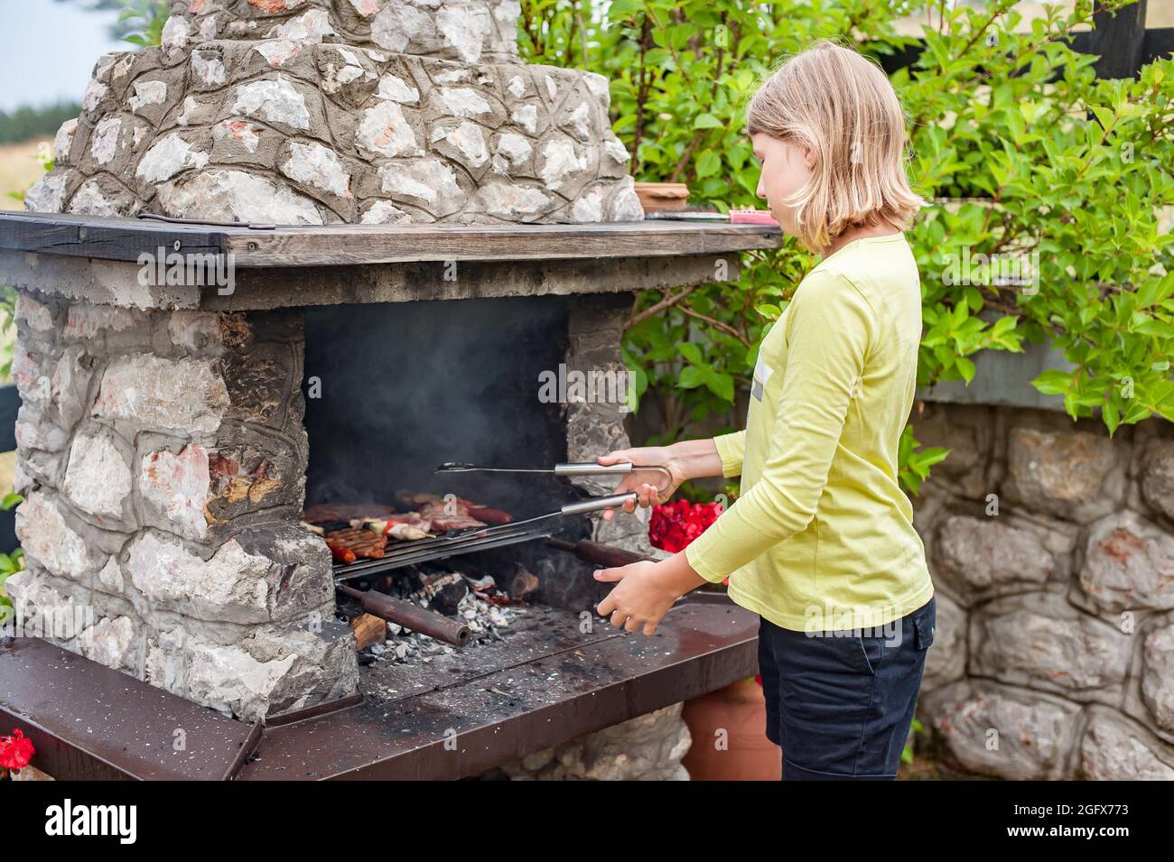 Children grilling meat. Happy teenage girl making barbecue on the grill ...