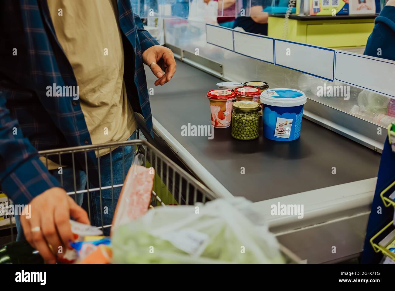 man lays out groceries from supermarket basket on conveyor belt ...