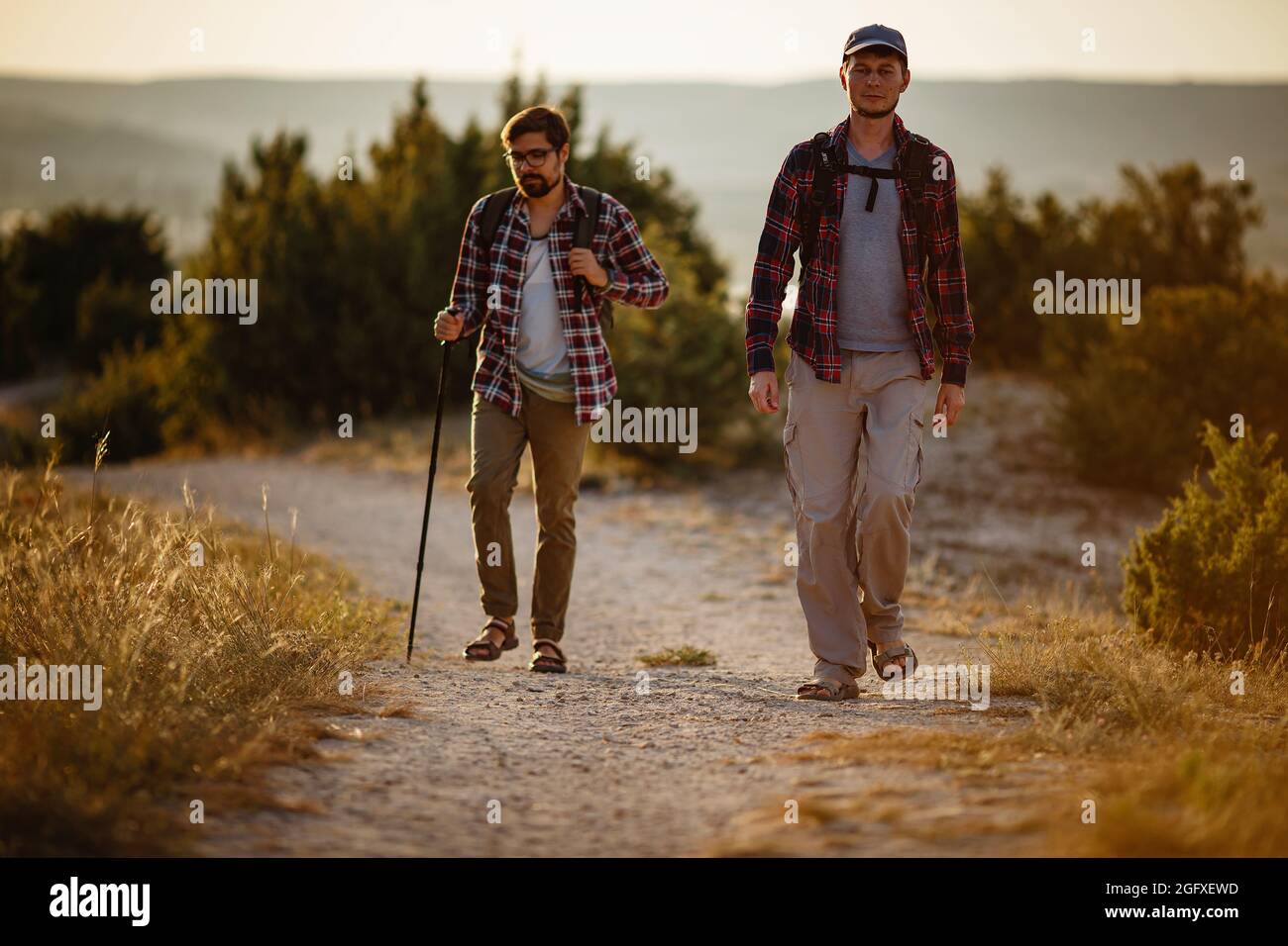 two men hikers enjoy a walk in nature, sunset time in summer. enjoying ...