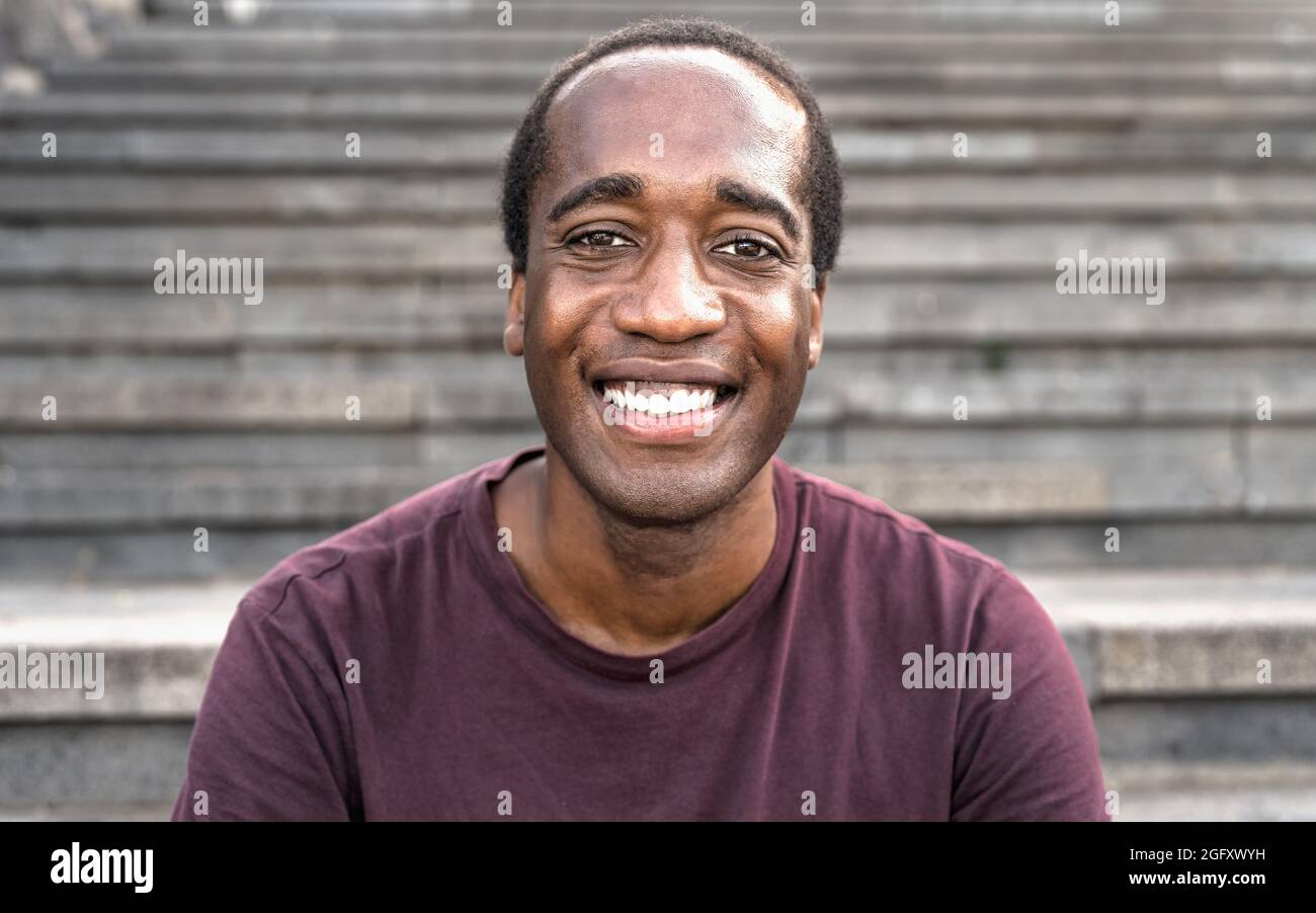 Happy African man smiling into the camera while sitting on urban stairs ...