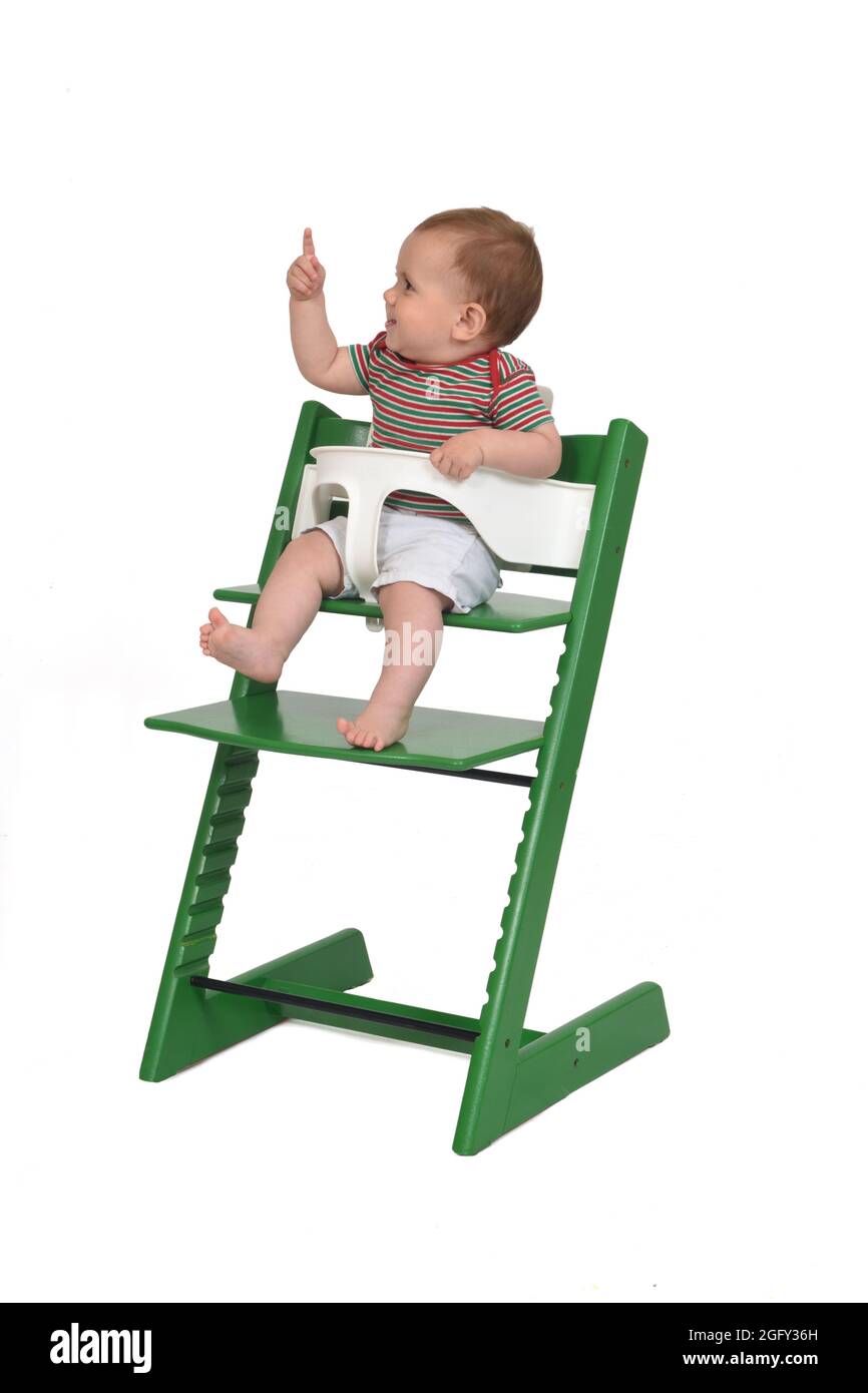 side view of a full portrait of a baby sitting in a highchair pointing ...