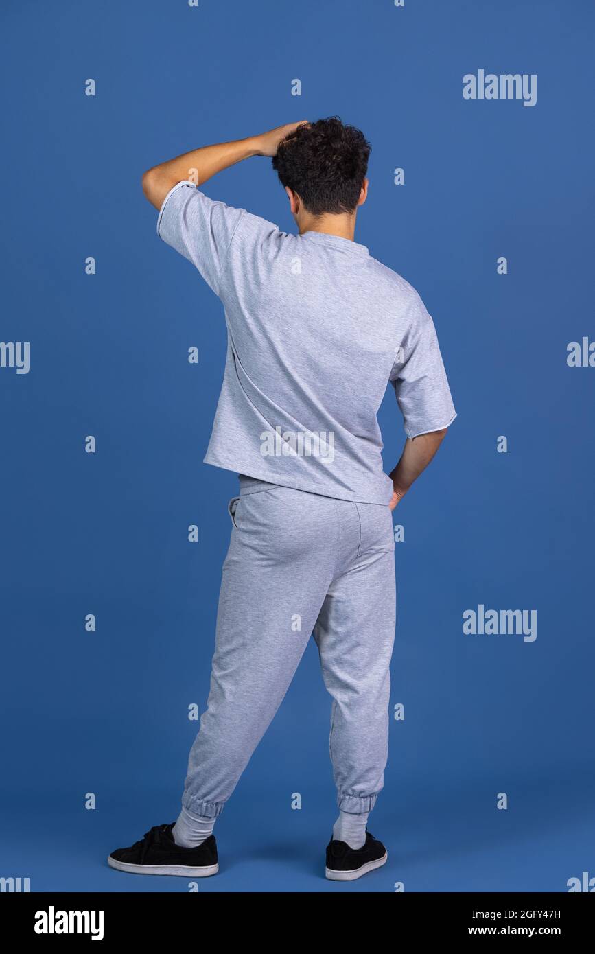 Back view of young curly man standing isolated over blue, navy studio ...