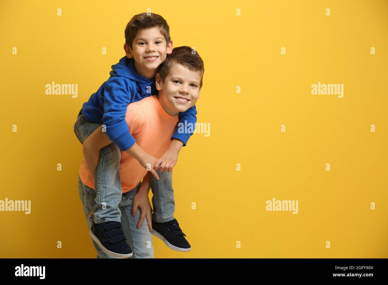 Cute little brothers standing on yellow background Stock Photo - Alamy