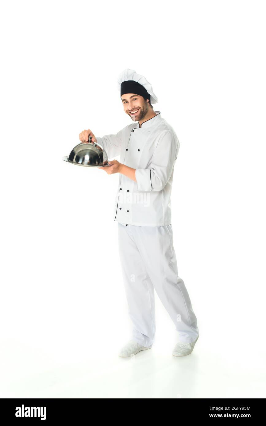 Full length of smiling chef holding cloche and tray on white background ...