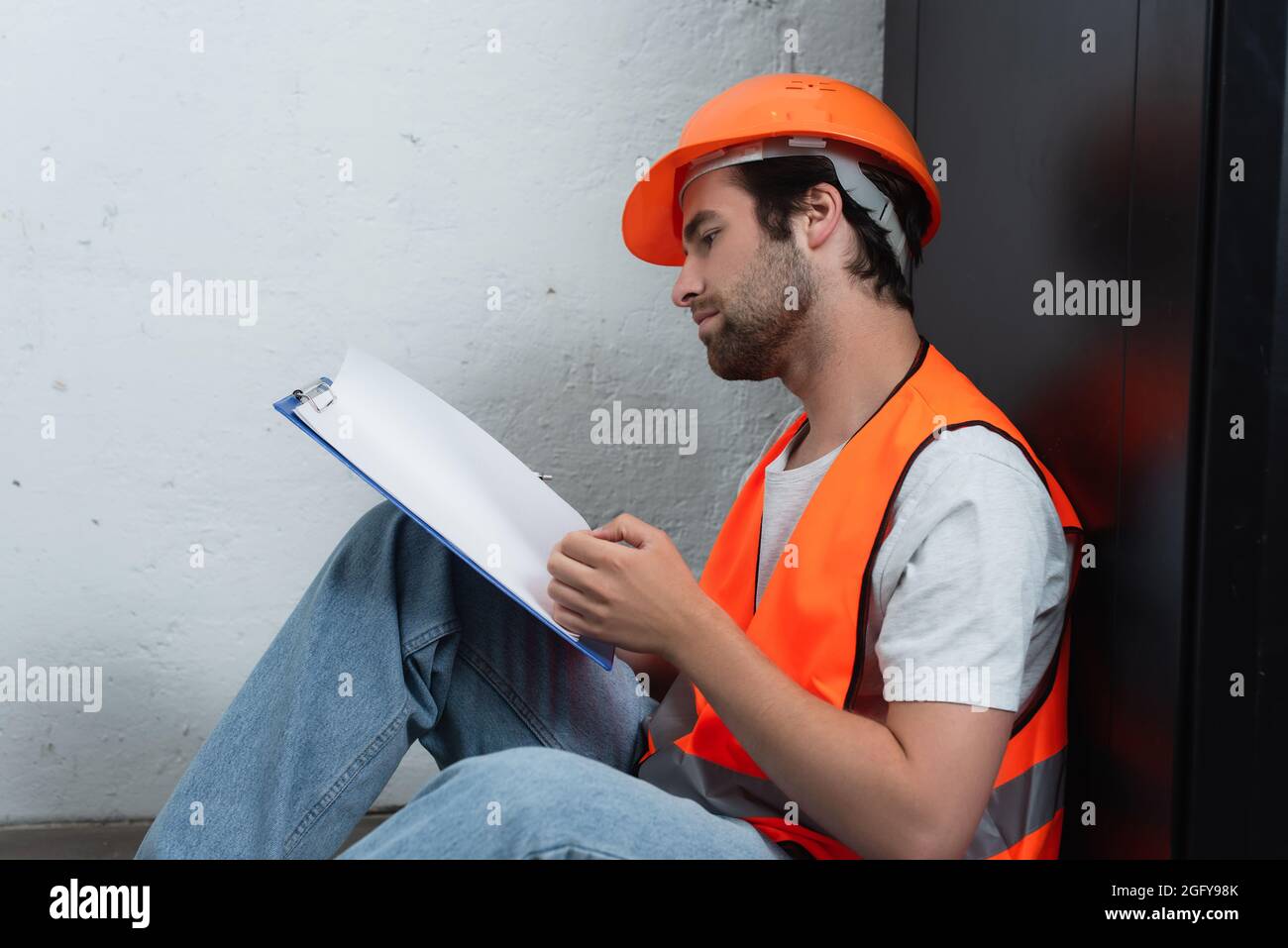 Side view of workman in hard hat looking at clipboard Stock Photo - Alamy