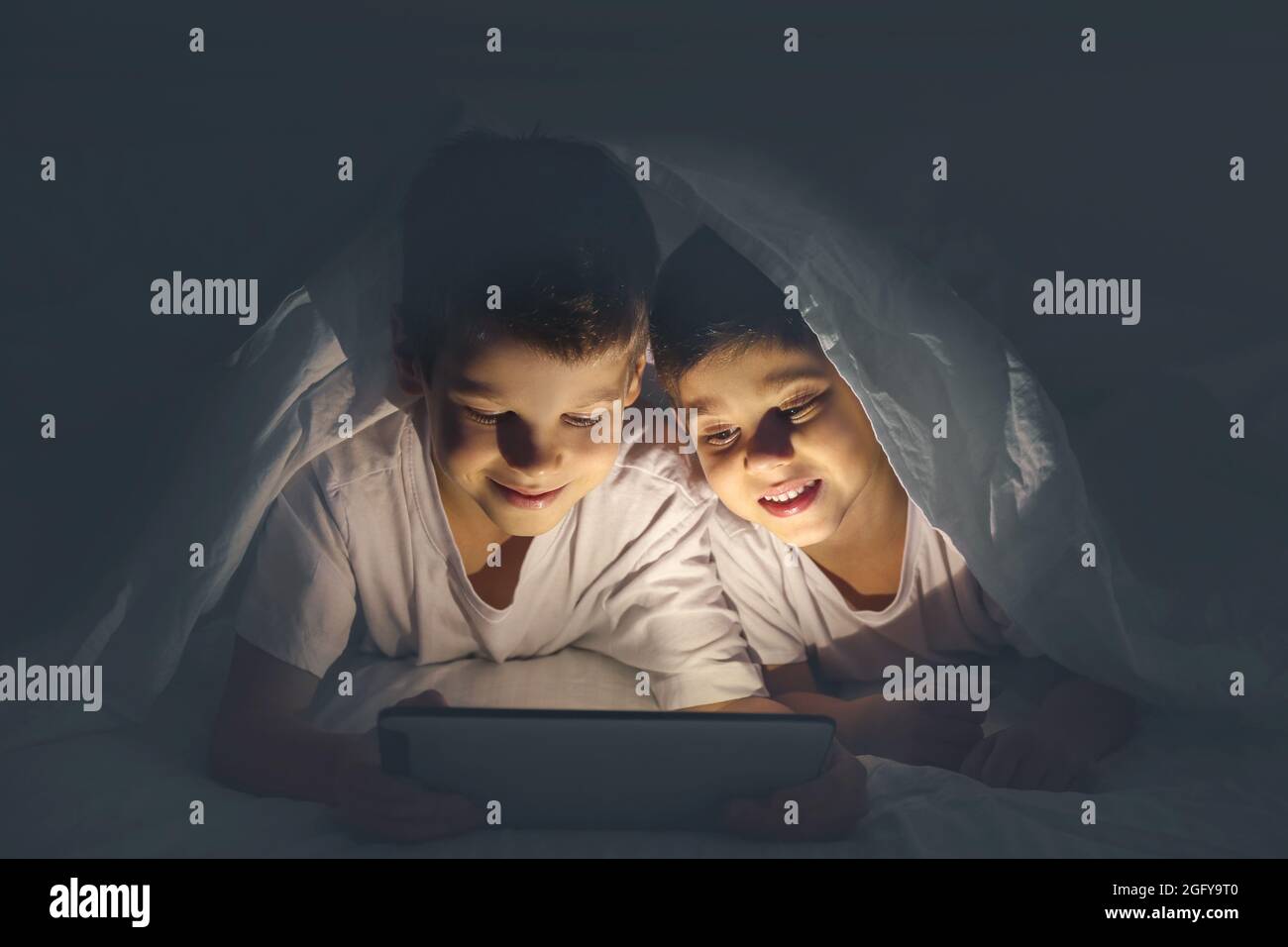Cute little brothers using gadget in bed under blanket, closeup Stock ...