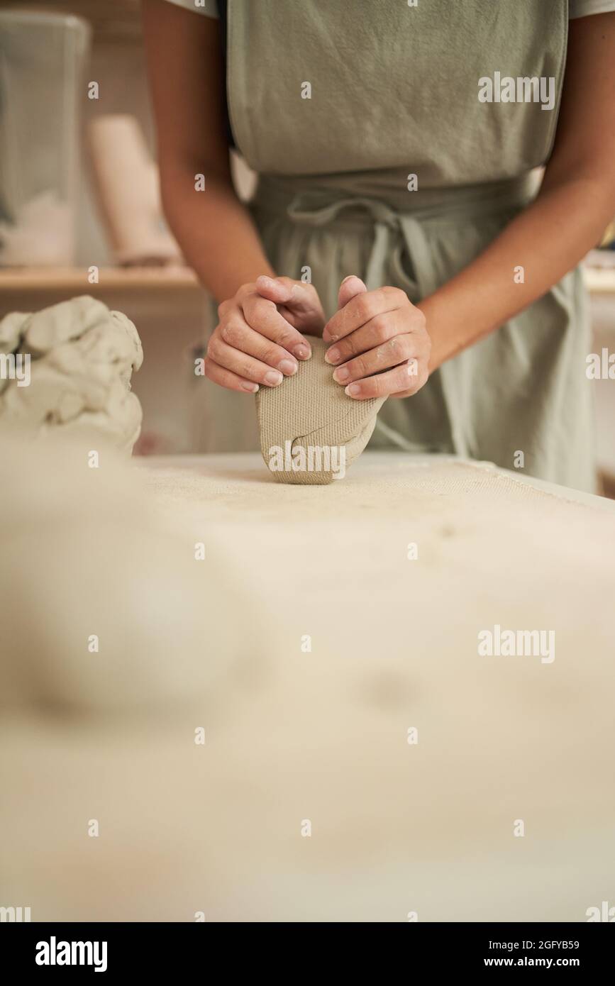 Unrecognizable craftswoman in apron kneading clay on workbench while ...
