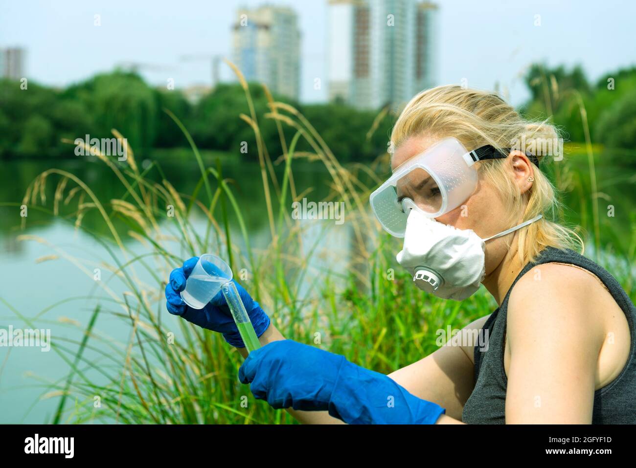 Woman with hands in gloves holds a glass with a sample of water ...
