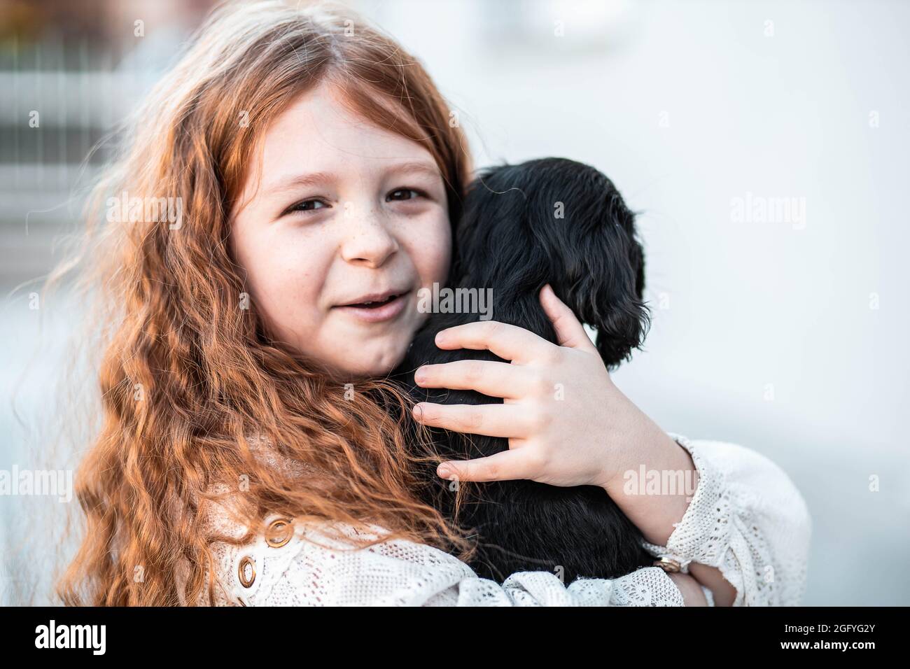 Little red hair freckled girl hugging her new friend, cute black puppy ...