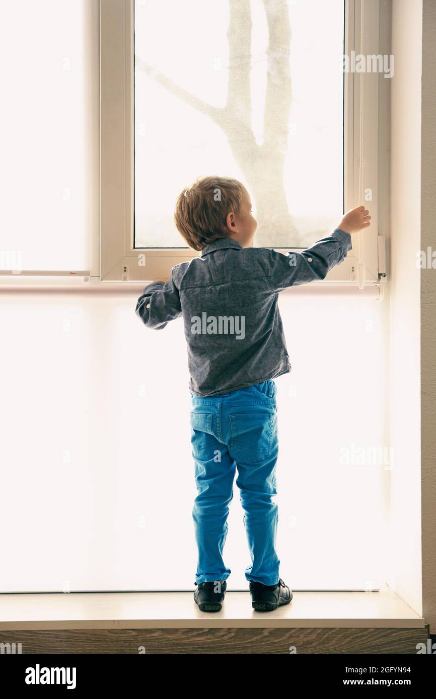 Cute little boy standing on window sill at home Stock Photo - Alamy
