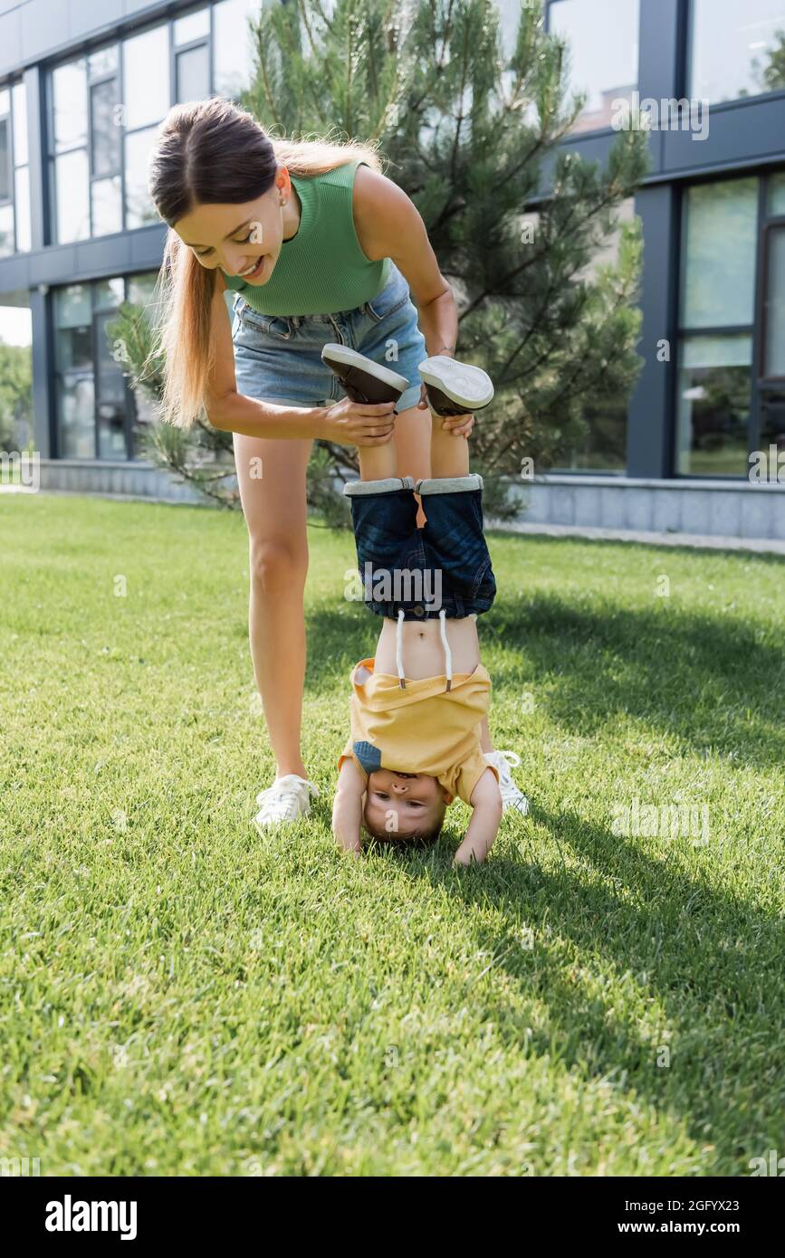 full length of happy mother supporting toddler son doing handstand ...