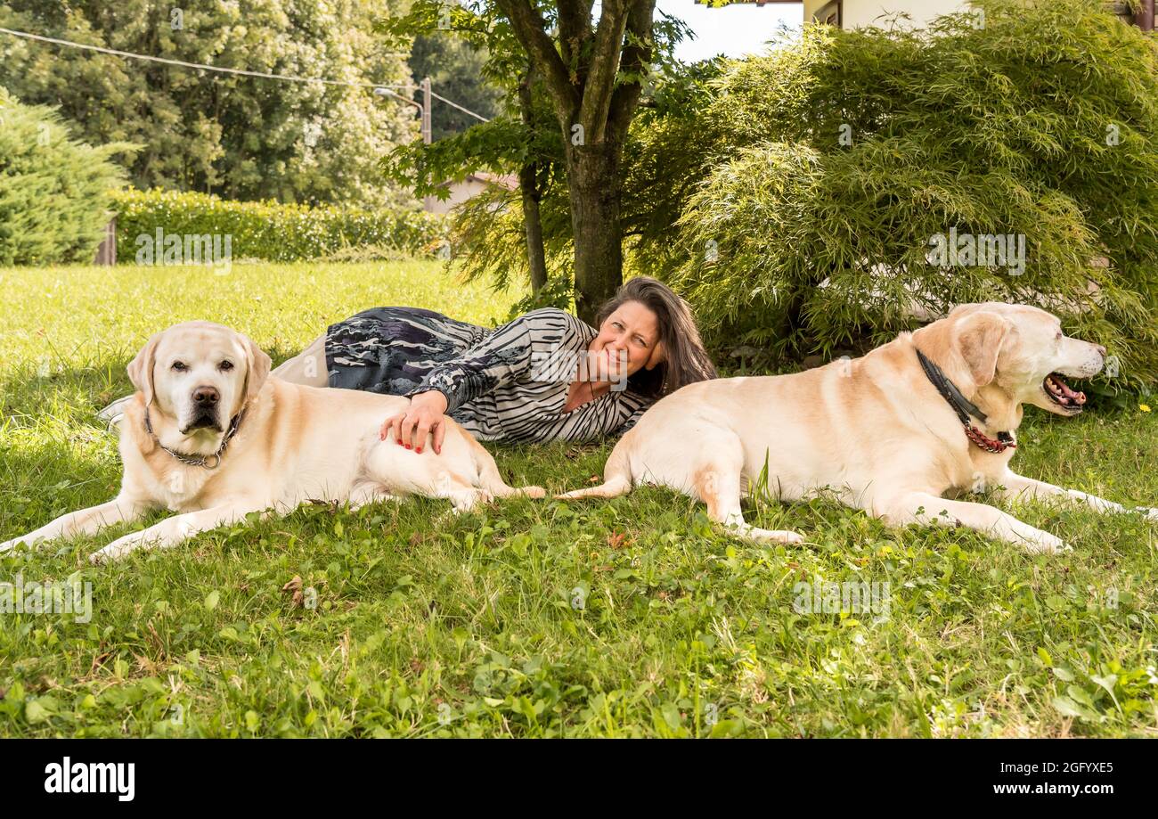 Happy mature woman with two labrador retriver dogs lying on the grass ...