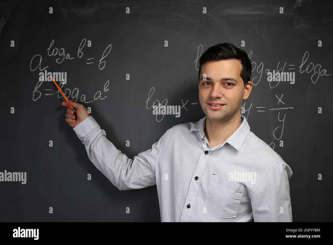 Handsome young teacher explaining math formulas written on blackboard ...