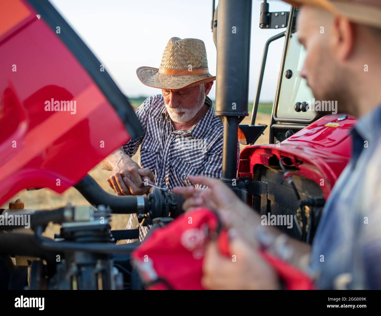 Two farmers repairing broken tractor in field during harvest work in ...