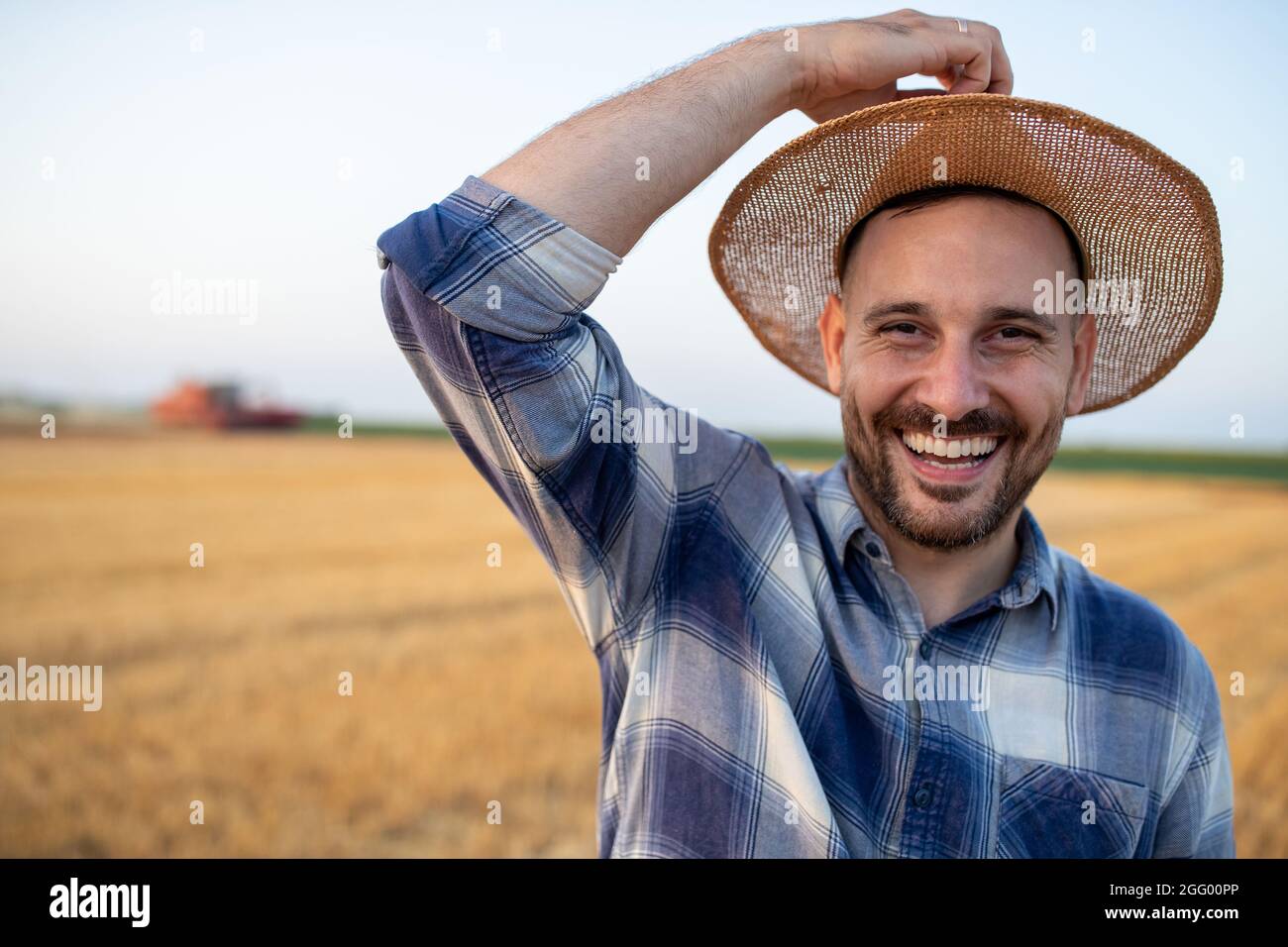 Satisfied handsome farmer smiling and holding straw hat on head in ...