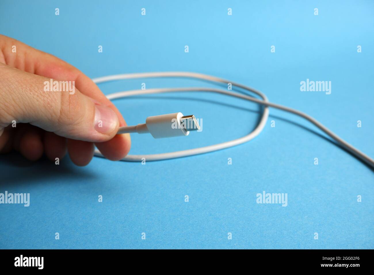 Fingers are holding a white usb cable with a type c interface on a blue ...