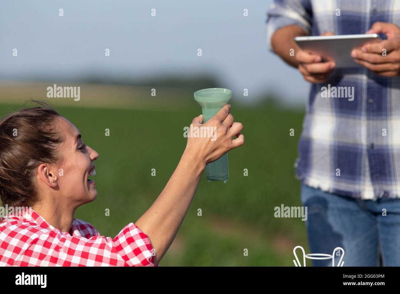 Young female farmer crouching in filed holding rain gauge smiling. Male ...