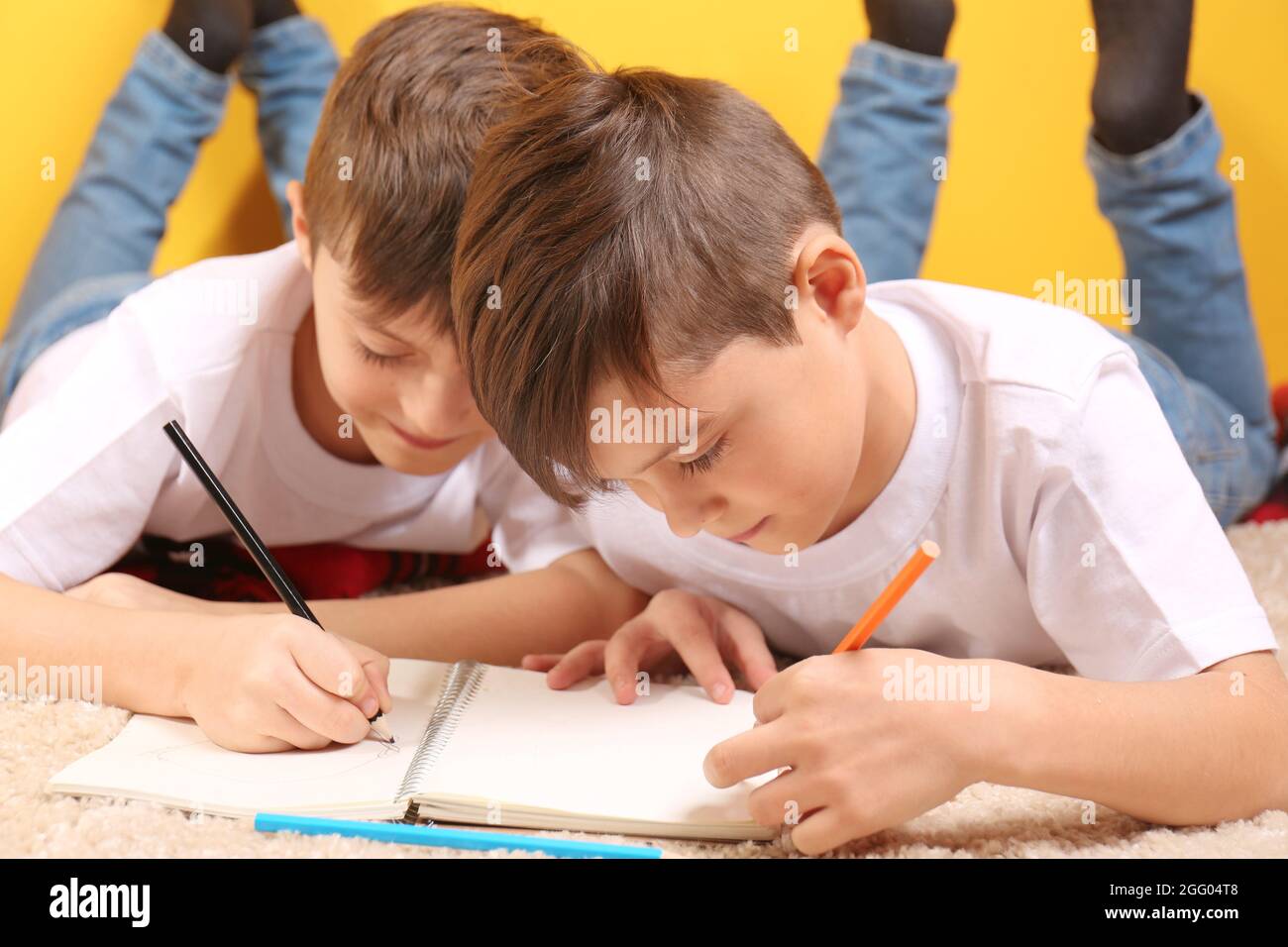 Twin brothers drawing in notebook on floor Stock Photo - Alamy