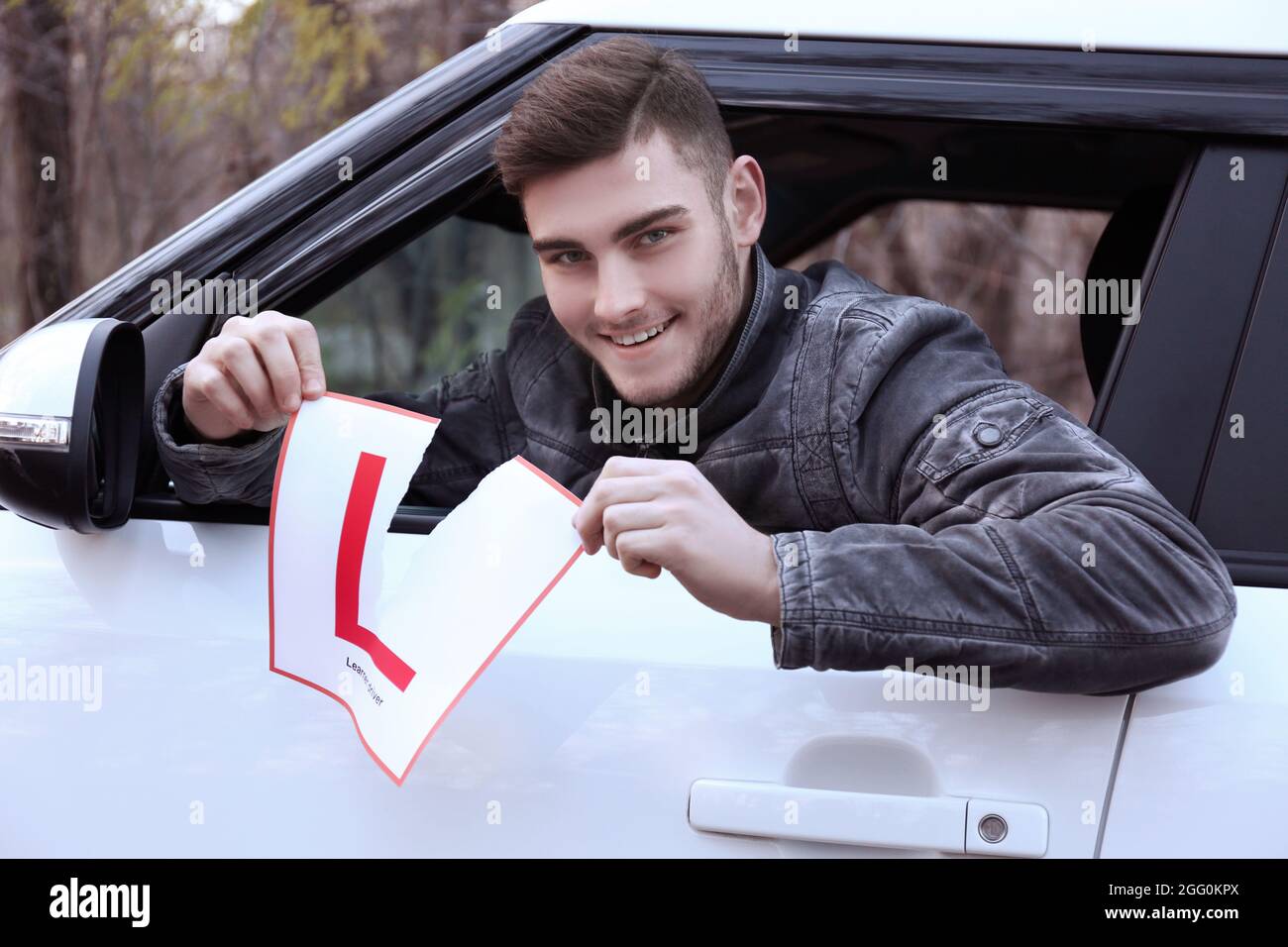 Young man tearing learner driver sign while looking out of car window ...