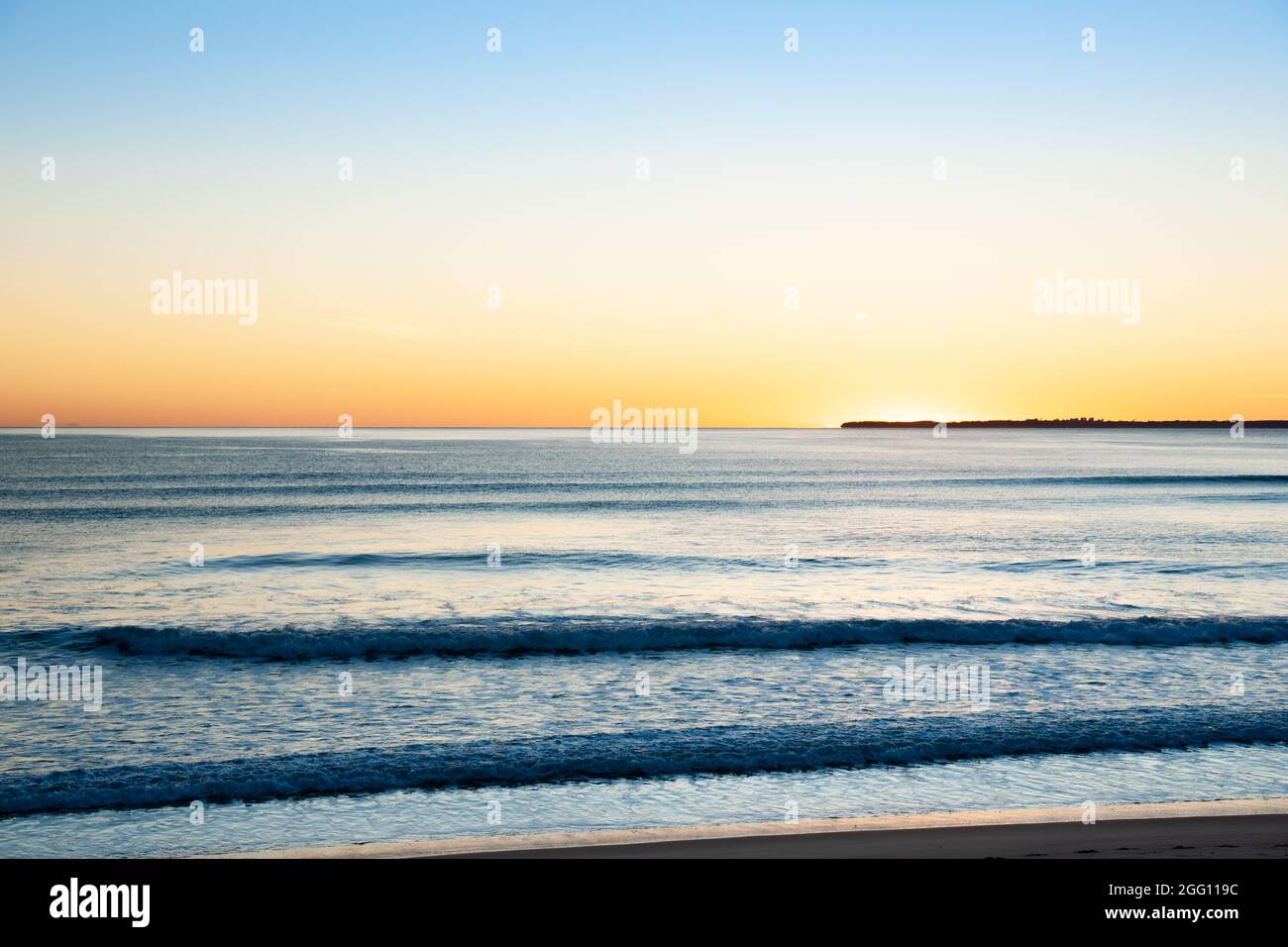 Sun rises casting a golden glow over low island on horizon across sea ...