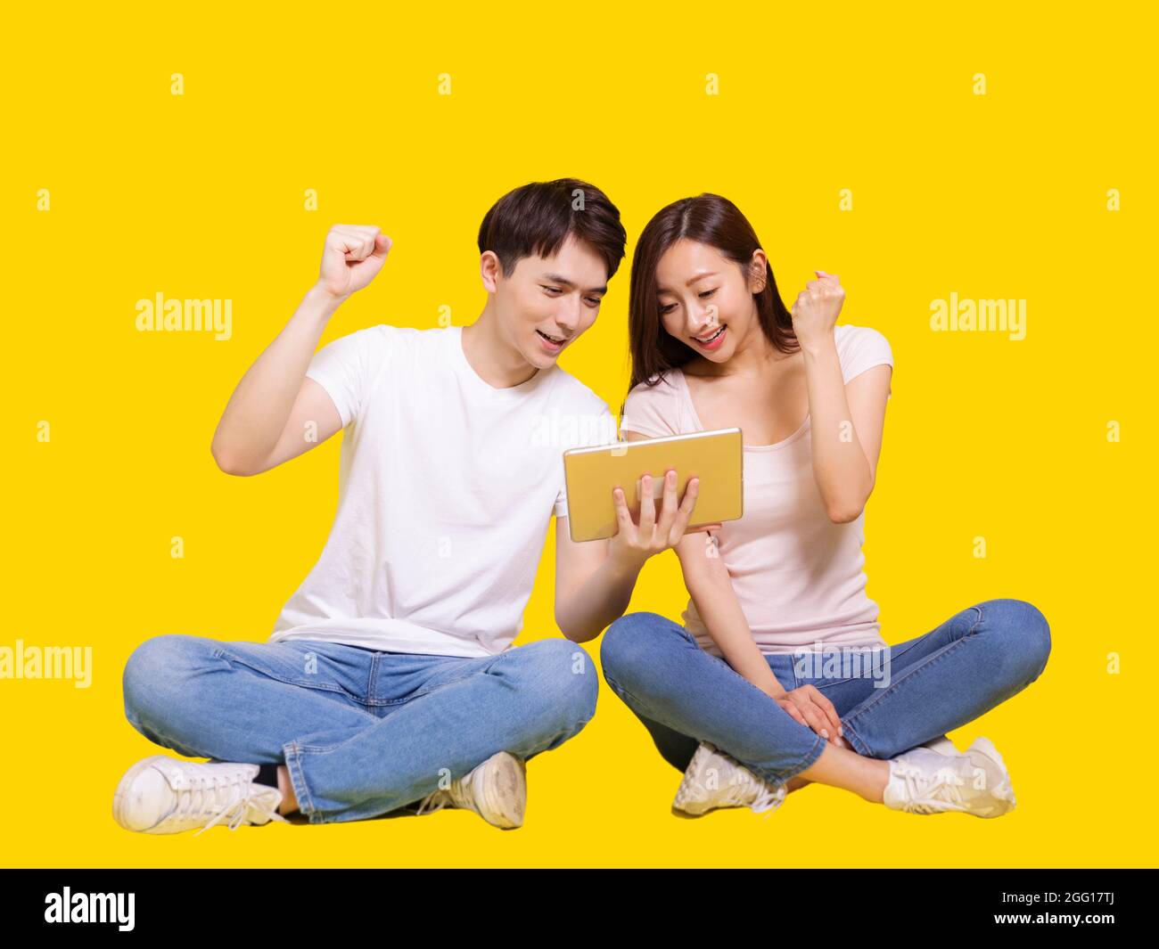 Happy young couple using tablet computer.Isolated on yellow background. Celebrating success ...