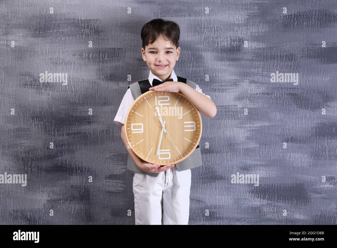 Cute little boy with big clock near color wall Stock Photo - Alamy