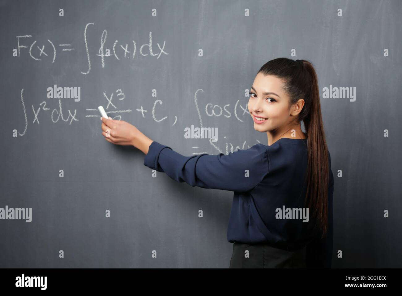 Beautiful young teacher explaining math formulas written on blackboard ...