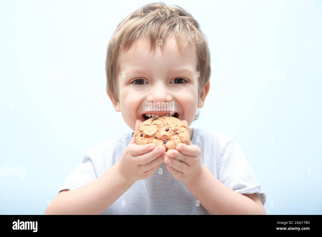 Cute little boy eating cookie on light background Stock Photo - Alamy