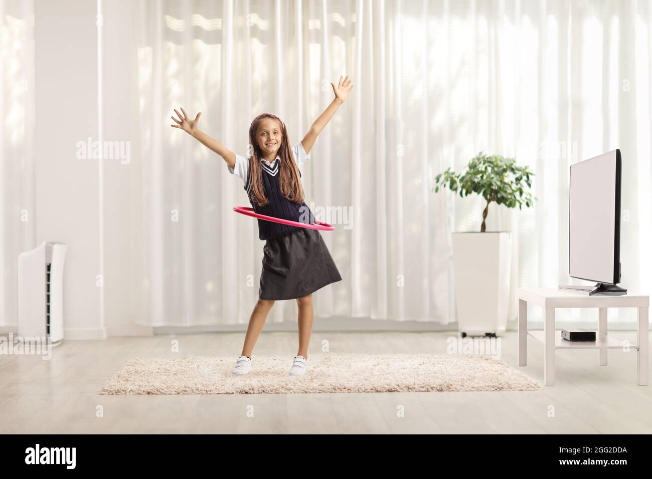 Playful schoolgirl dancing with a hula hoop at home in a living room ...