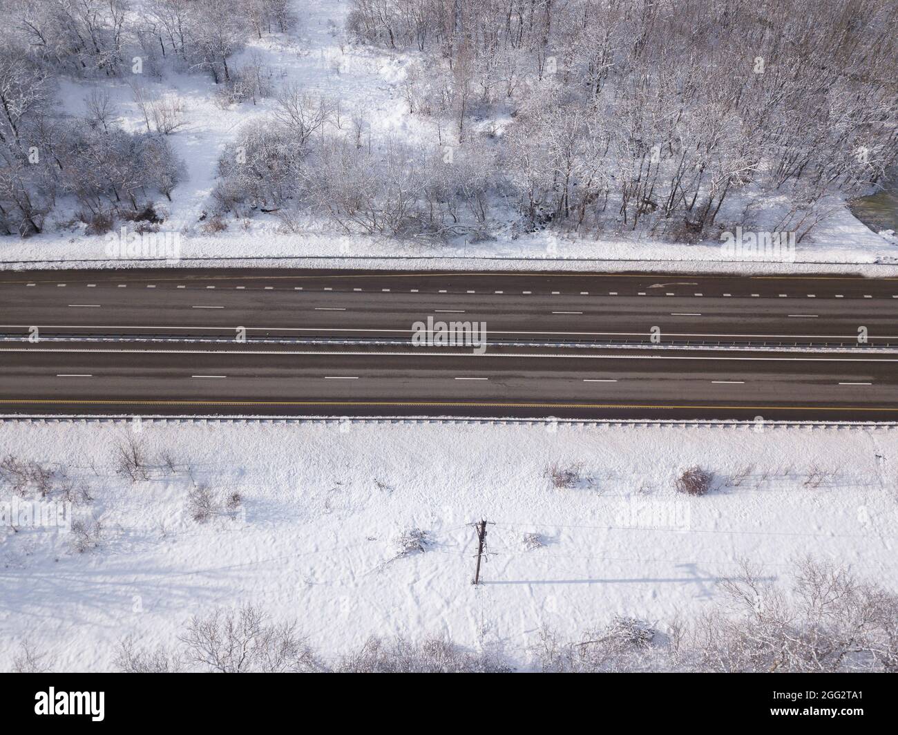 Night time aerial top down view of a snowy road surrounded pine tree ...