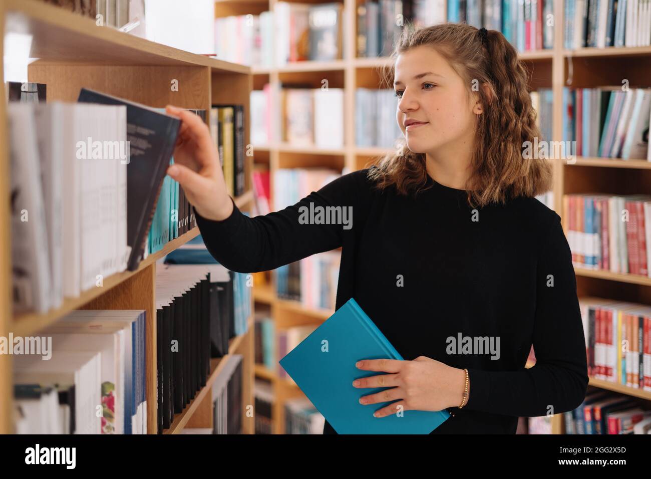 Happy tenage girl or student taking book from shelf in library - People ...