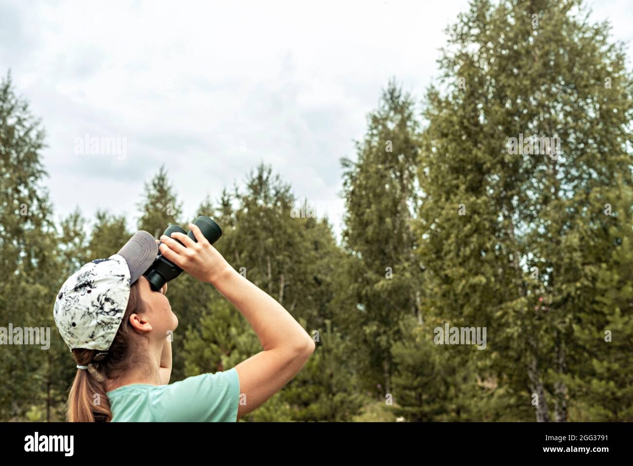 Young blonde woman bird watcher in cap and blue looking through ...