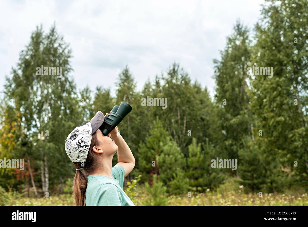 Young blonde woman bird watcher in cap and blue looking through ...