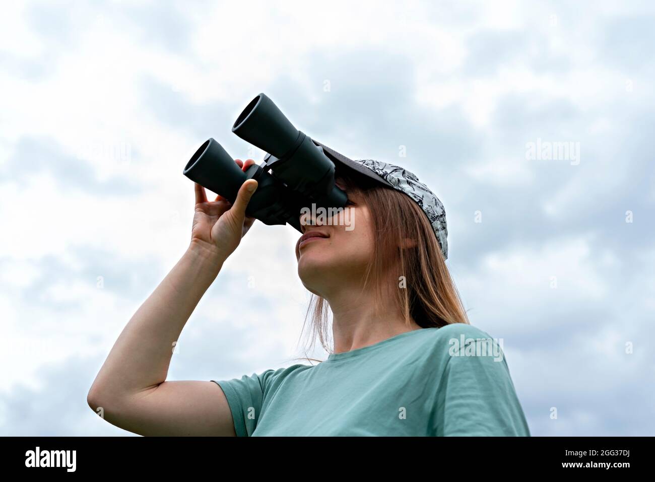 Young blonde woman bird watcher in cap and blue looking through ...