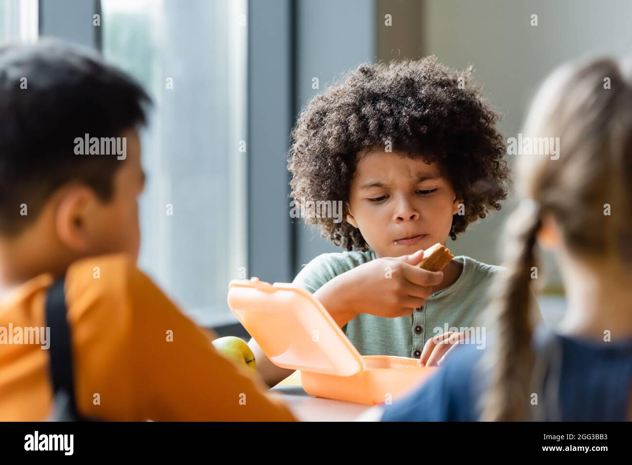 african american boy eating sandwiches near blurred classmates Stock ...