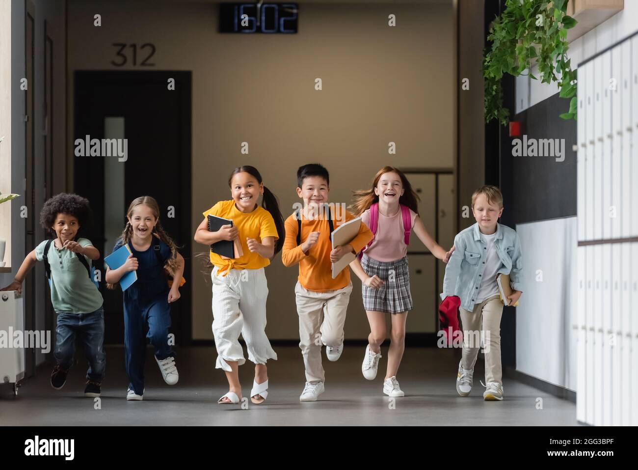 joyful multicultural friends with notebooks running in school corridor ...