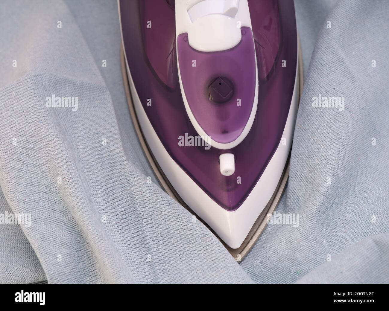 A violet iron ironing blue linen textile Stock Photo - Alamy