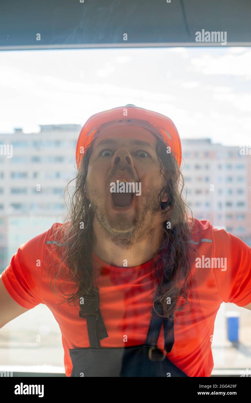 funny engineer in a helmet makes a face behind the glass Stock Photo ...