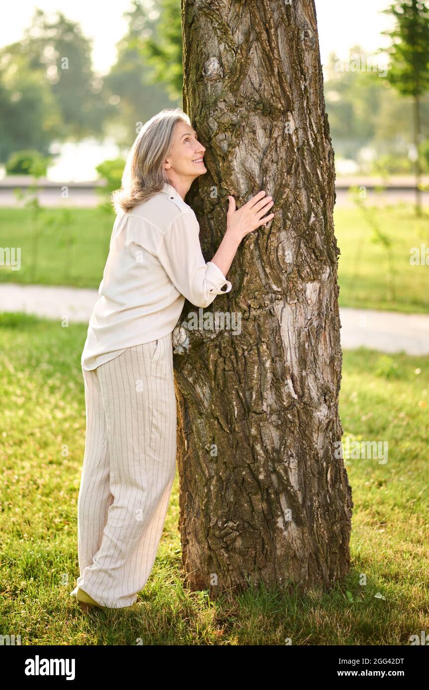 Woman leaning against tree in green park Stock Photo - Alamy