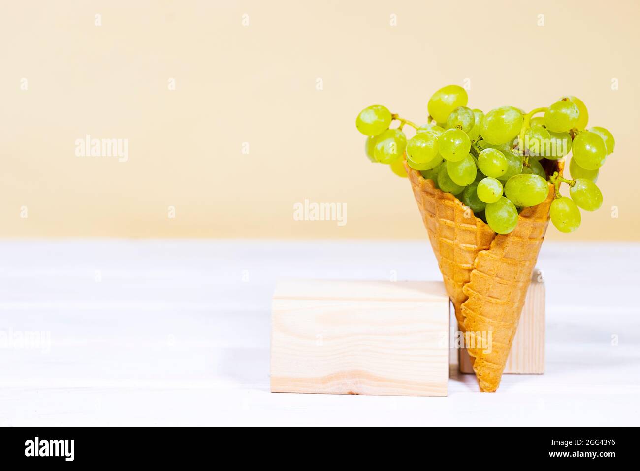 Green grape in sweet wafer cone on wooden stands over light orange ...