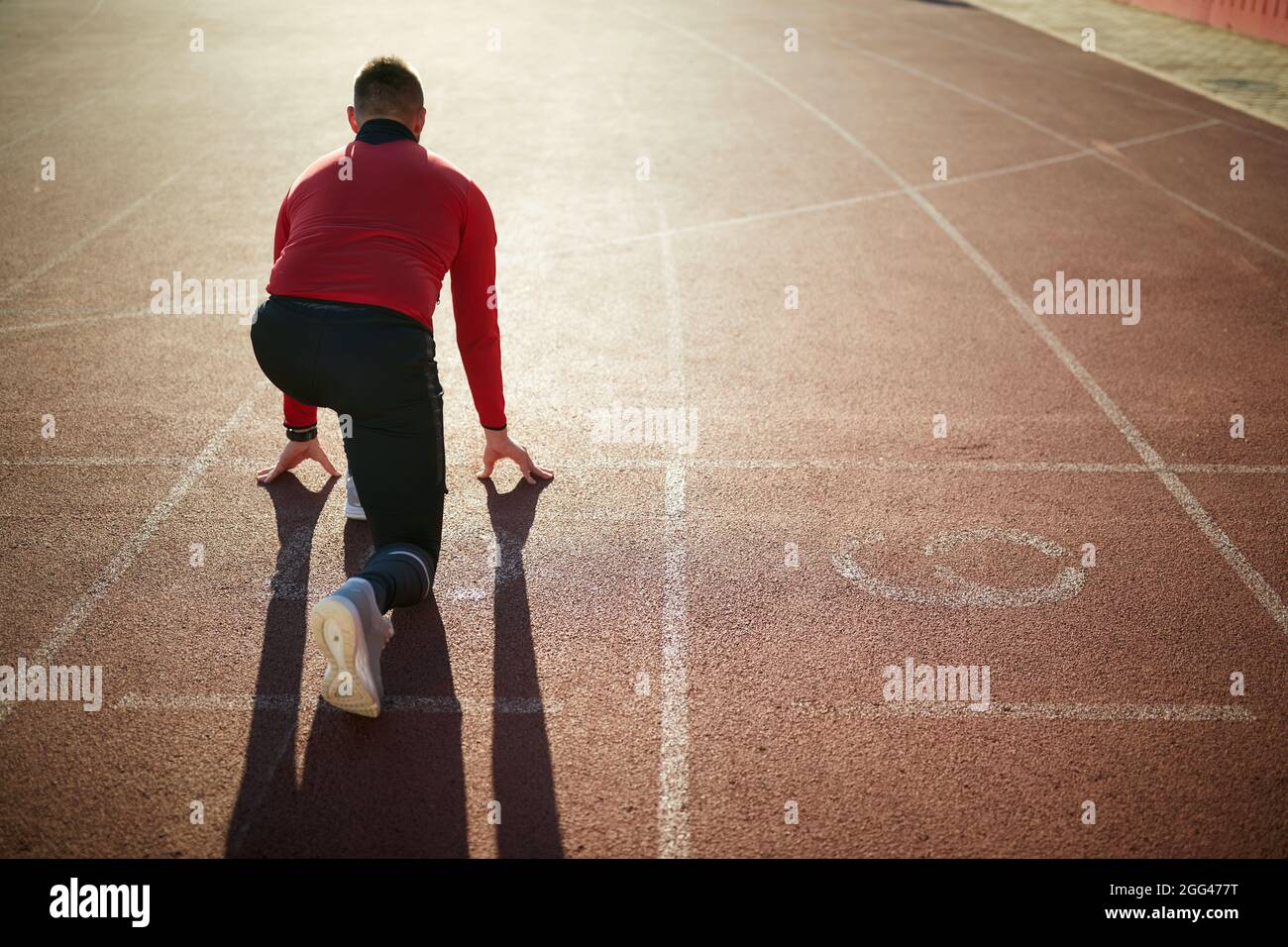 Young man sprinters at starting position ready for race on racetrack ...