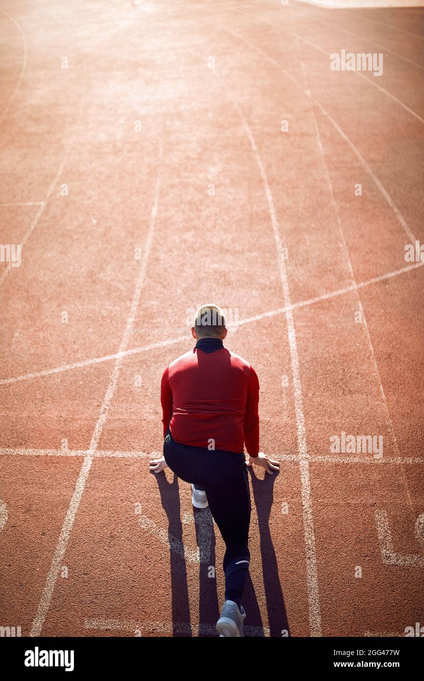Back view of young man in starting position for running on race track ...