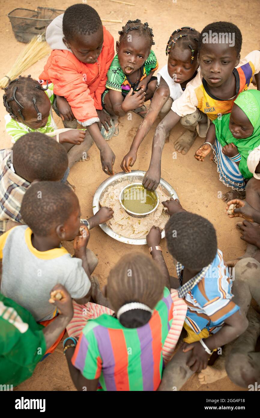 A group of children eat around a communal dish of millet paste and ...
