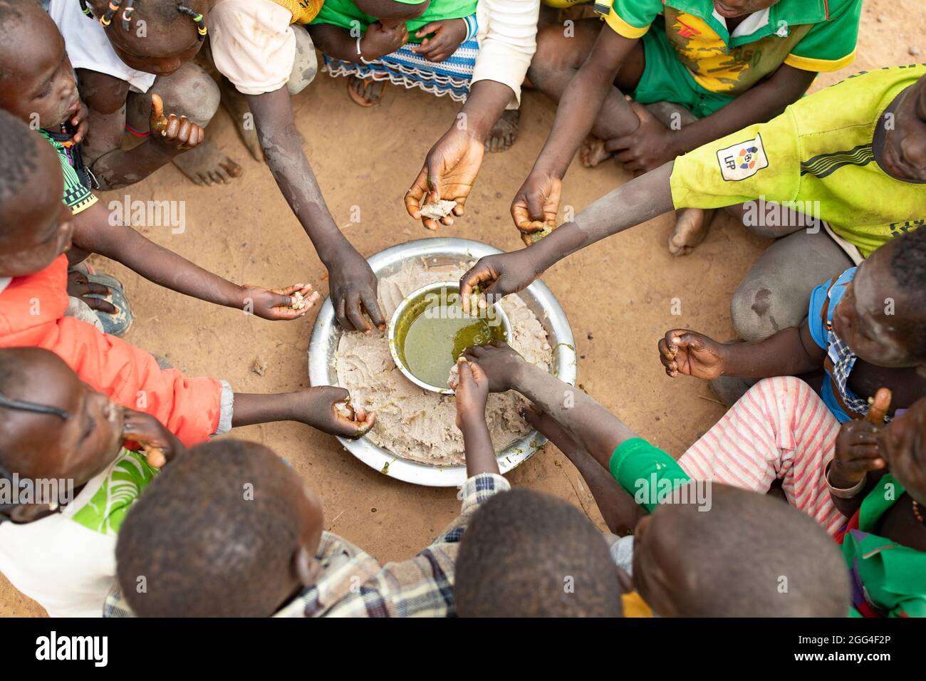 A group of children eat around a communal dish of millet paste and ...