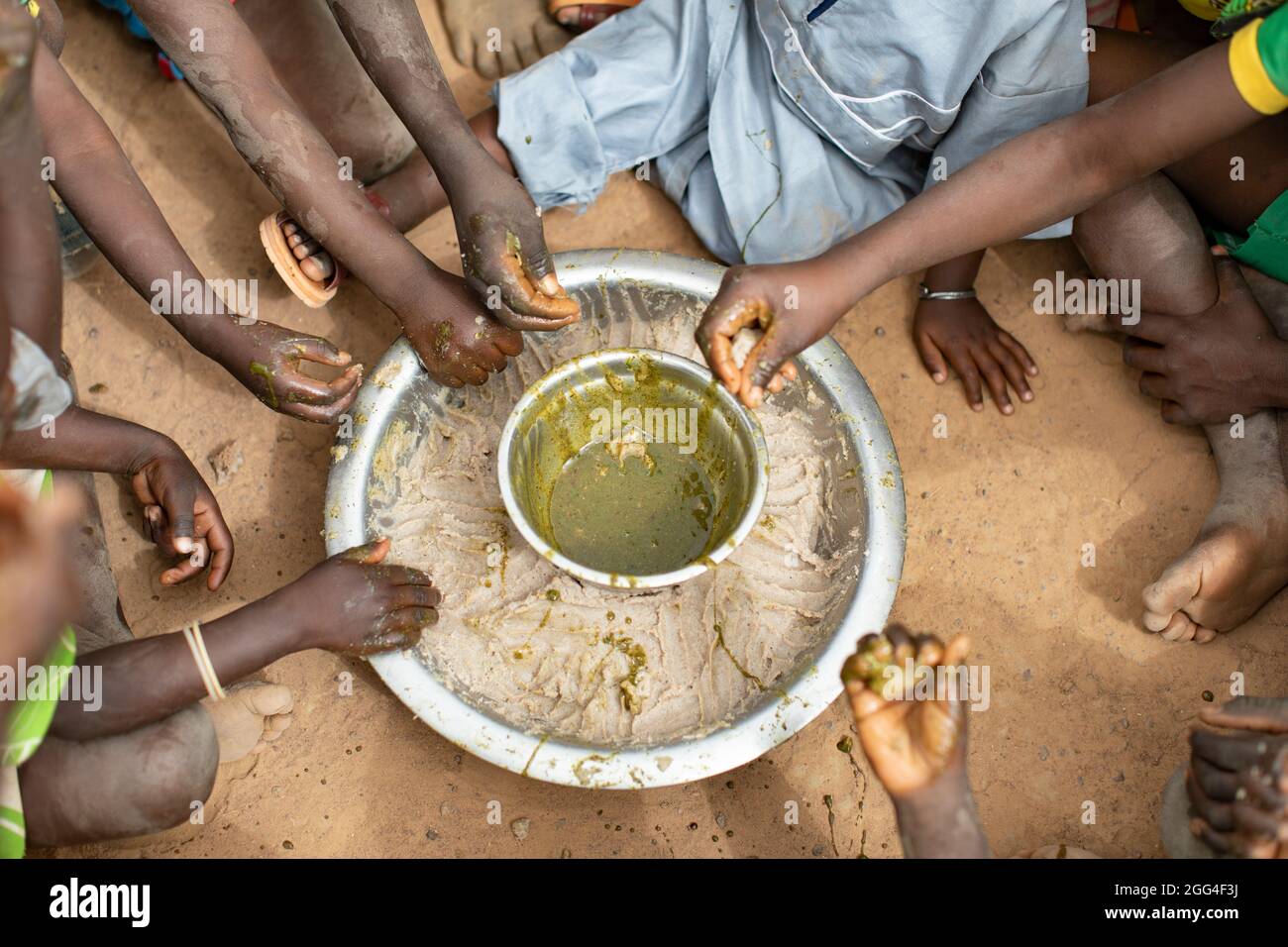 A group of children eat around a communal dish of millet paste and ...