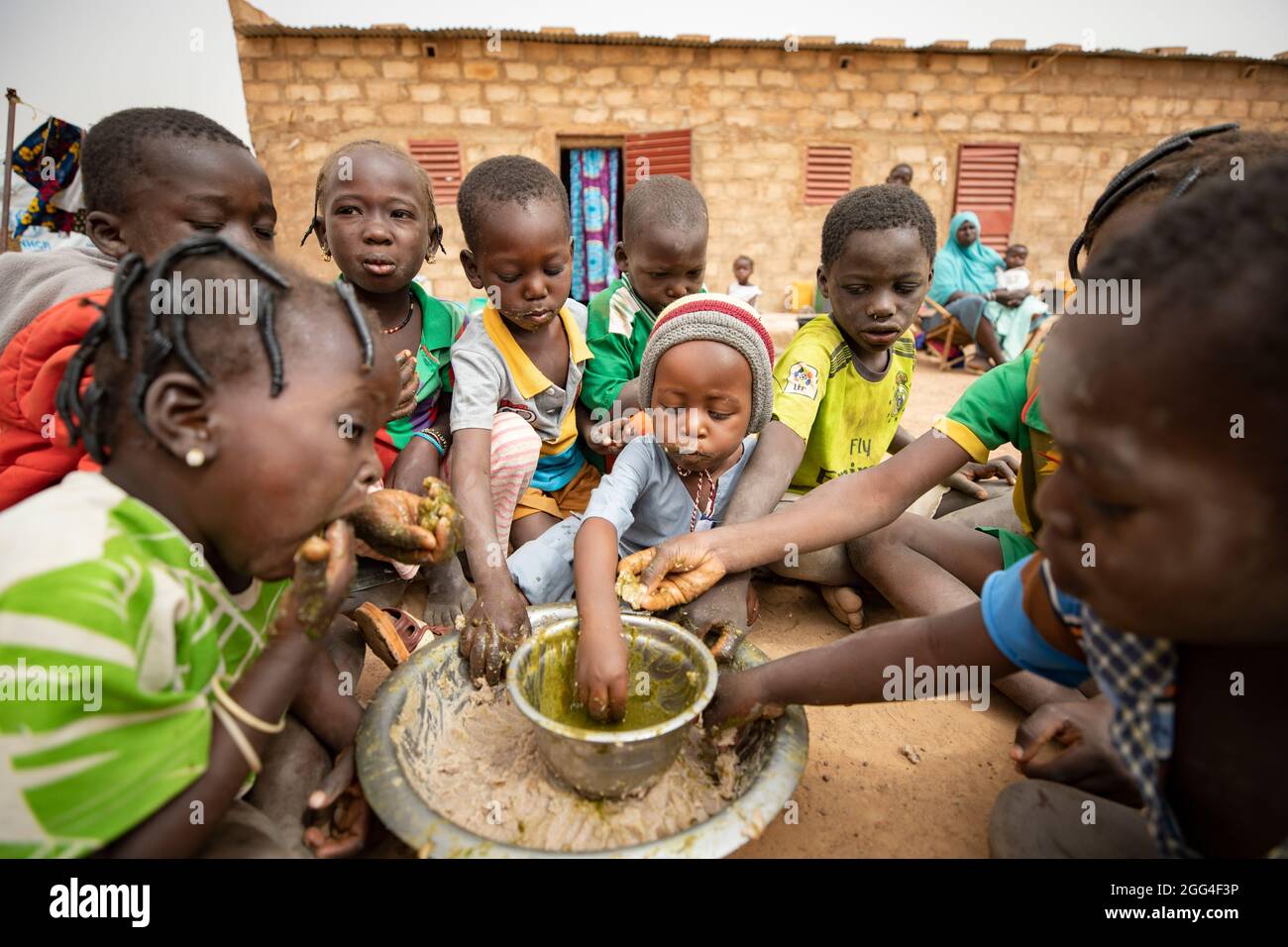 A group of children eat around a communal dish of millet paste and ...