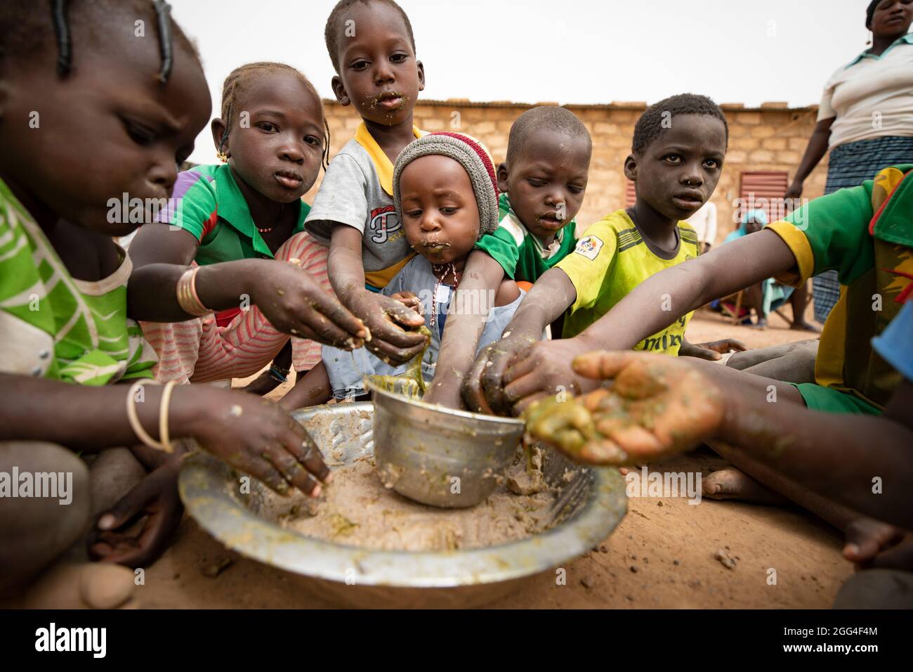 A group of children eat around a communal dish of millet paste and ...