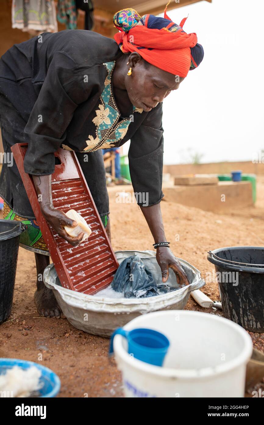 A woman washes clothes using a washboard and basin outside her home in ...