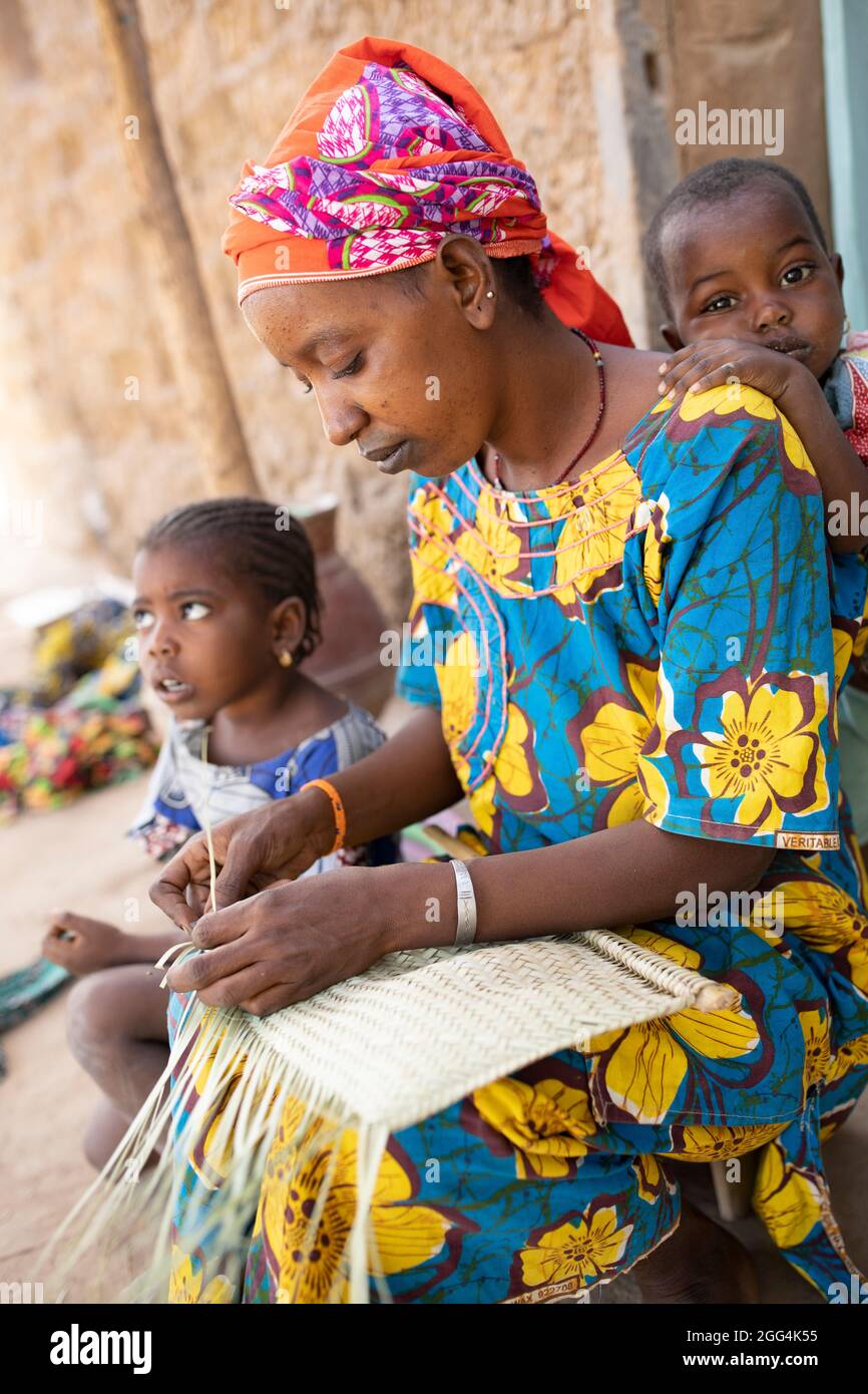 A Fulani mother weaves matts and fans from dried palm fronds by hand ...
